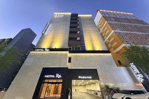 Hotel com destaque para a placa 'HOTEL RIL', entrada de estacionamento e fachada moderna.