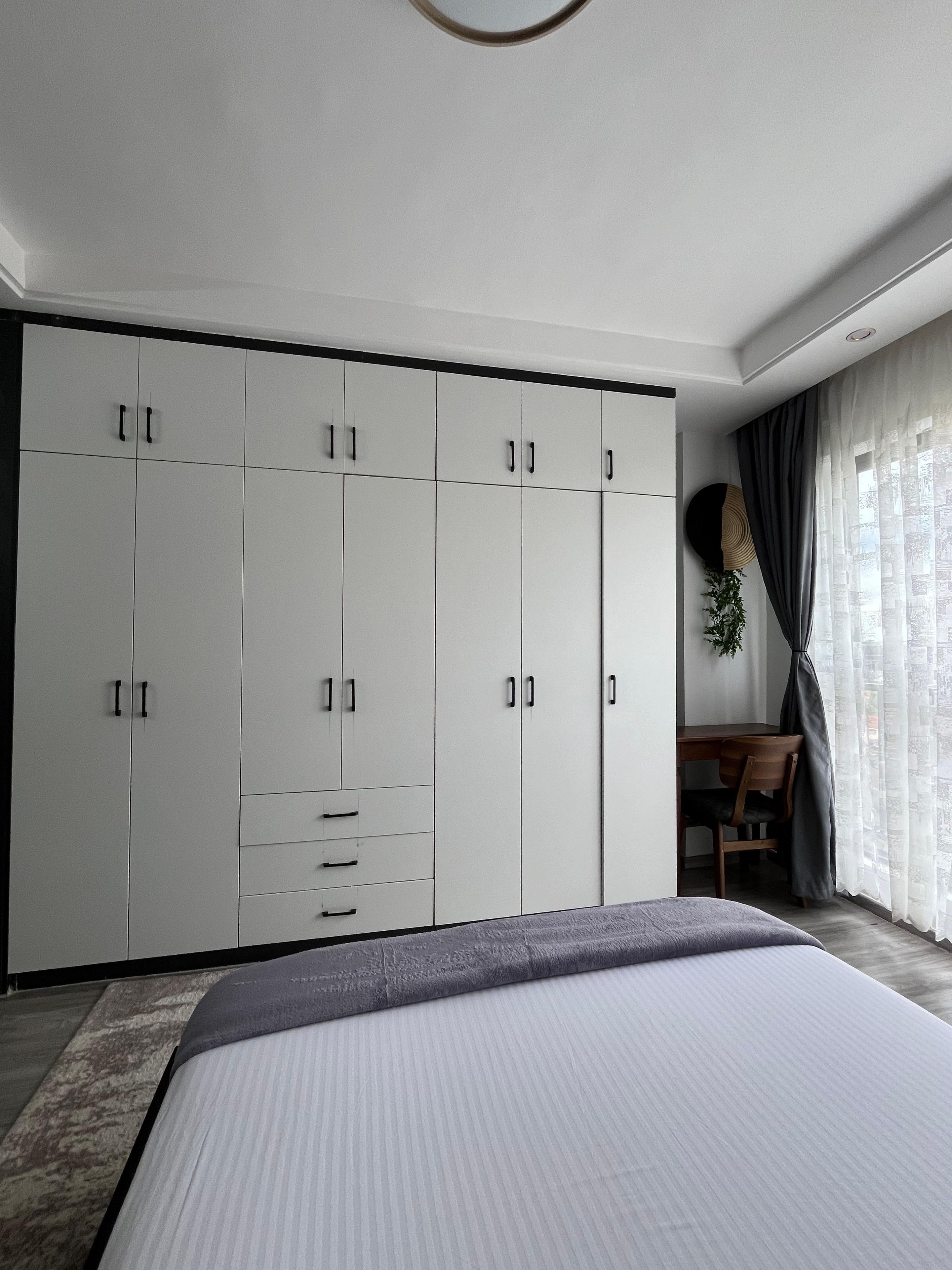 Quarto com uma cama grande, um guarda-roupa com vários compartimentos, uma escrivaninha e uma cadeira.