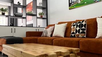 Uma sala de estar moderna com um sofá marrom, uma mesa de centro de madeira, uma estante preta com objetos decorativos e uma pintura de cães jogando sinuca.