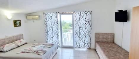 Quarto com cama, um banco, uma televisão e janela com cortinas.
