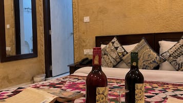 Quarto de hotel com uma cama, duas garrafas de vinho, um suporte com copos e um tapete colorido.