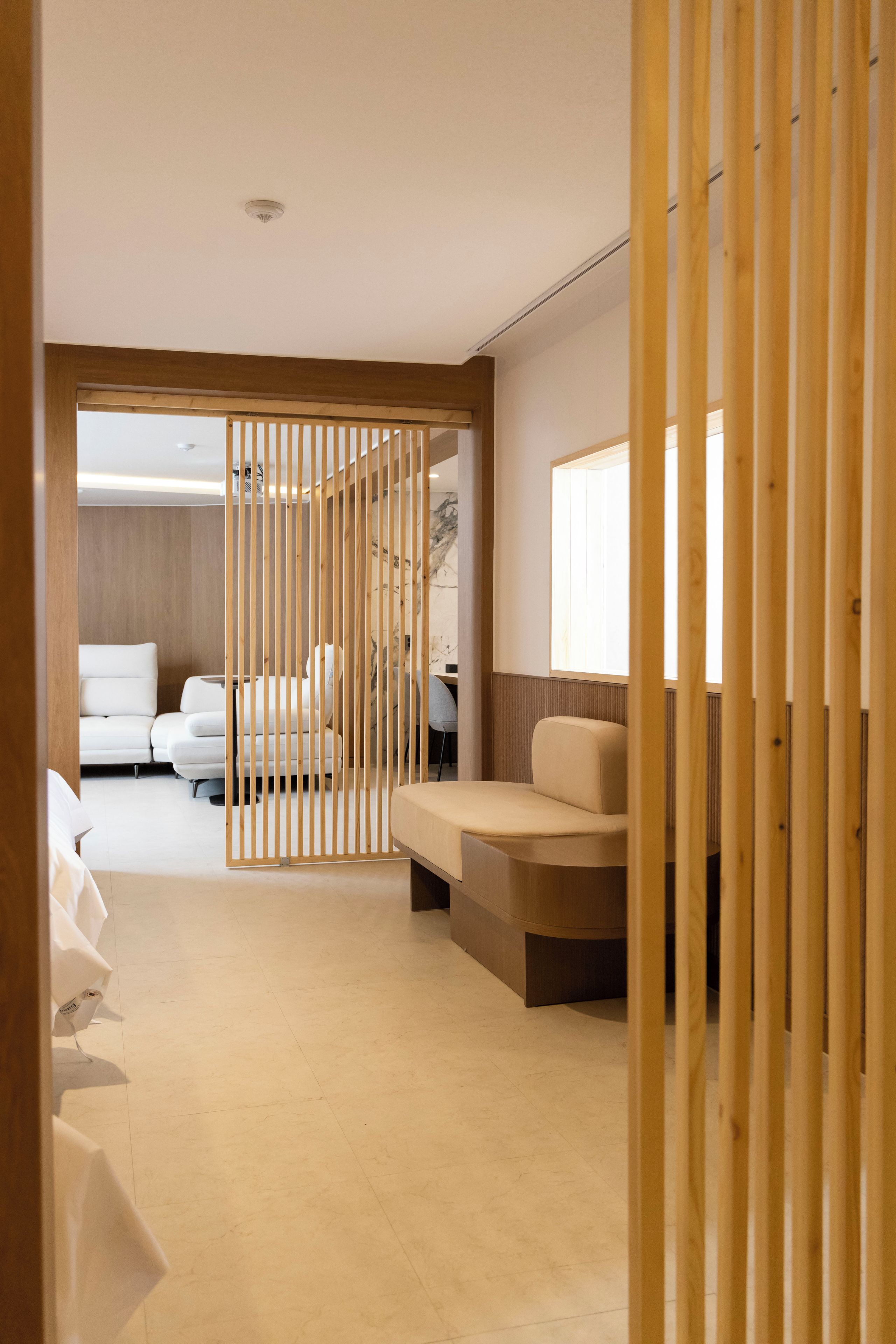 Quarto de hotel moderno com divisória de madeira, sofá, cama e janela.