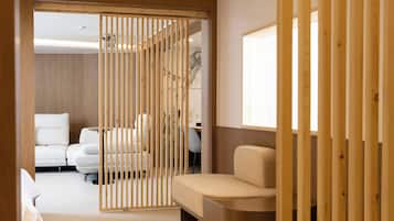 Quarto de hotel moderno com divisória de madeira, sofá, cama e janela.