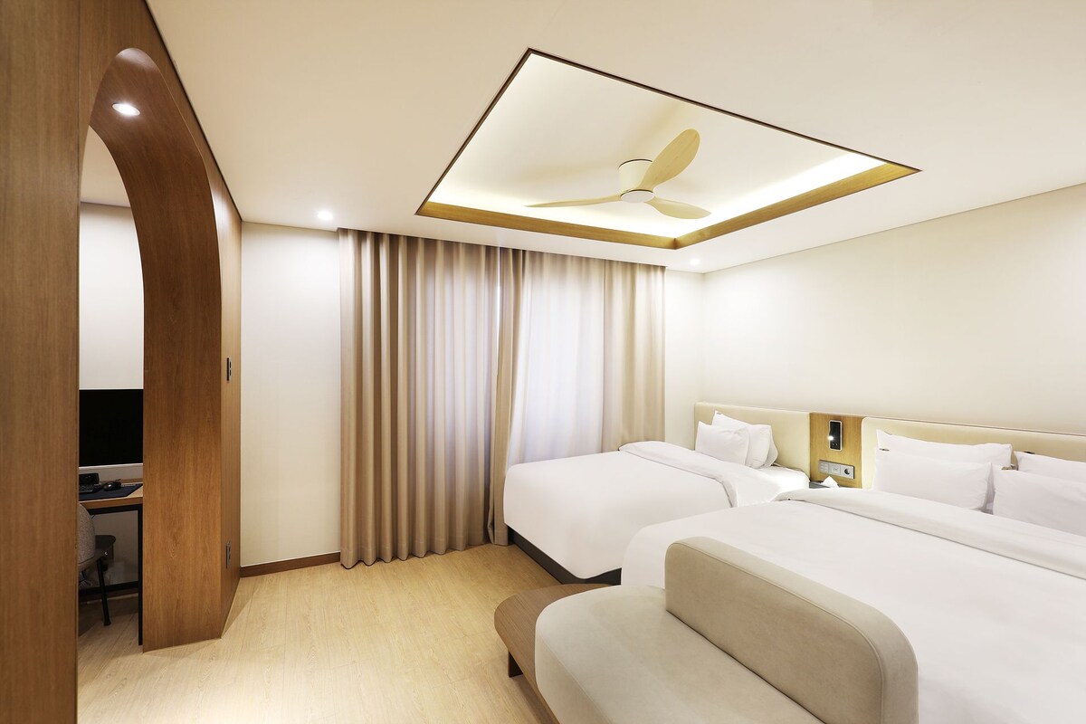 Quarto de hotel com cama, escrivaninha e ventilador de teto.