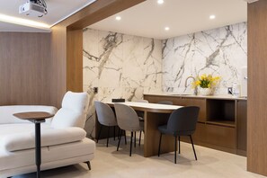 Cozinha moderna com painel de fundo de mármore, área de refeições com sofá e cadeiras brancas e uma pequena ilha com pia e flores.