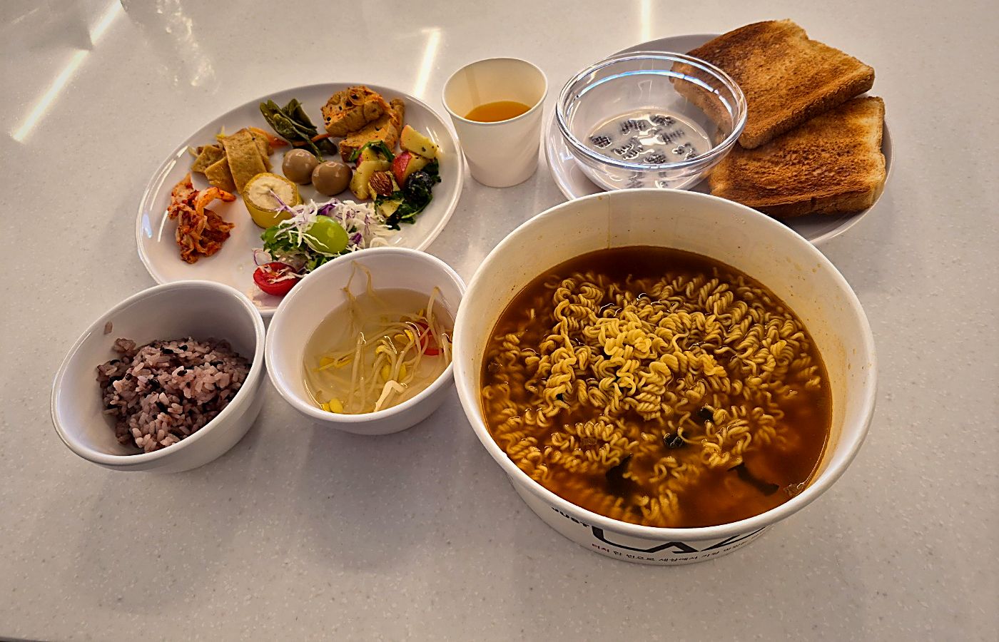 Uma mesa com diversos pratos, incluindo ramen, arroz e legumes.