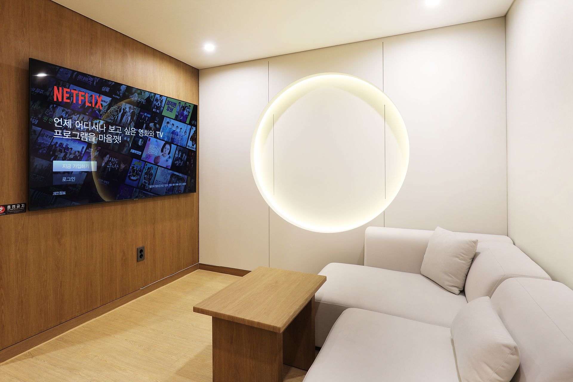 Uma sala de estar moderna com televisão de tela plana fixada numa parede de madeira, uma luminária de teto redonda e um sofá branco.