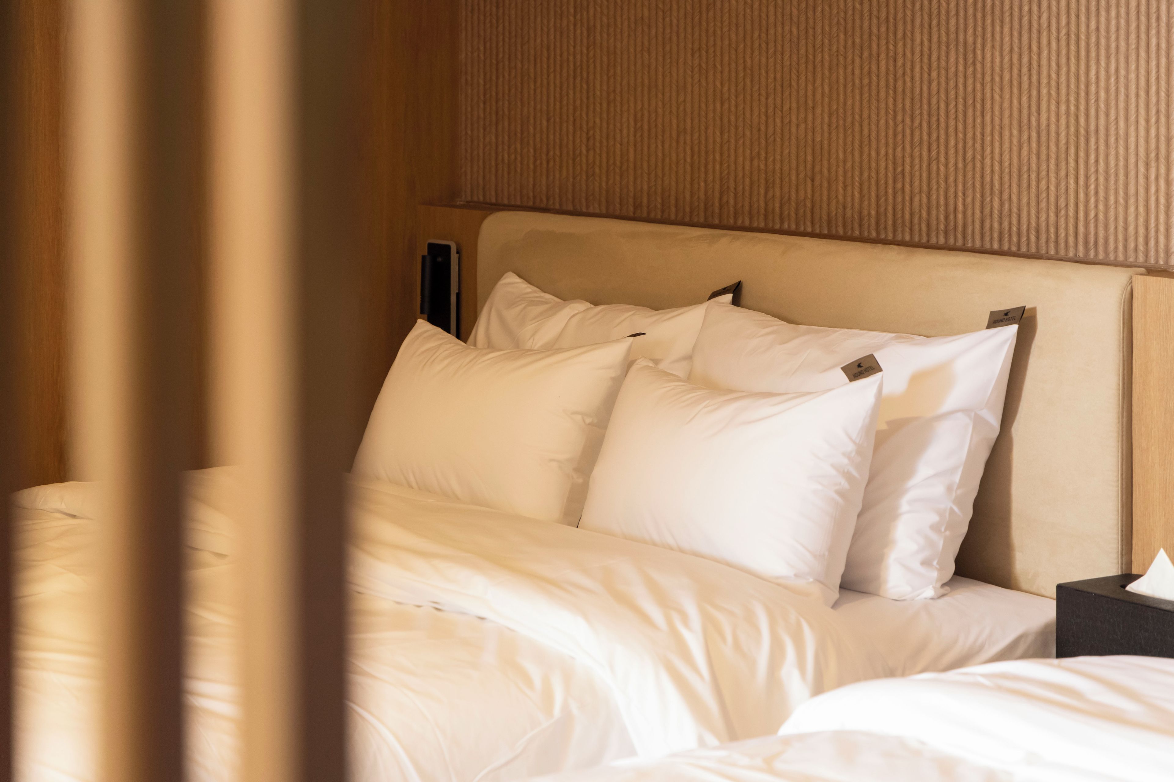 Quarto de hotel com cama, almofadas, mesa de cabeceira e telefone fixado na parede.