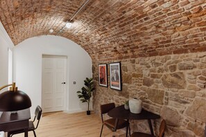 Quarto com parede de pedra, porta branca, mesa com cadeiras e um vaso de planta.