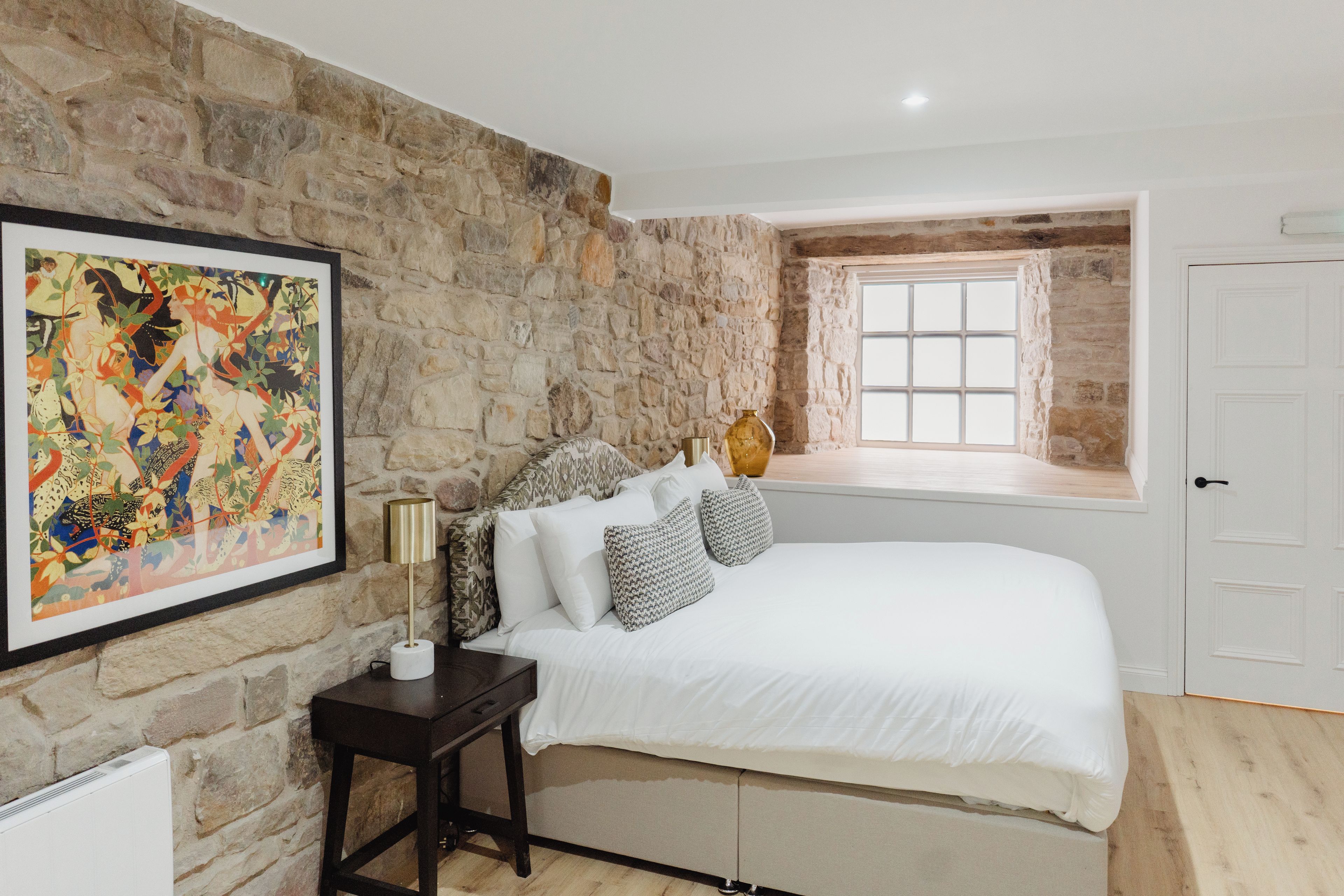 Quarto com parede de pedra, uma cama grande, uma janela e um quadro pendurado na parede.