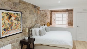 Quarto com parede de pedra, uma cama grande, uma janela e um quadro pendurado na parede.