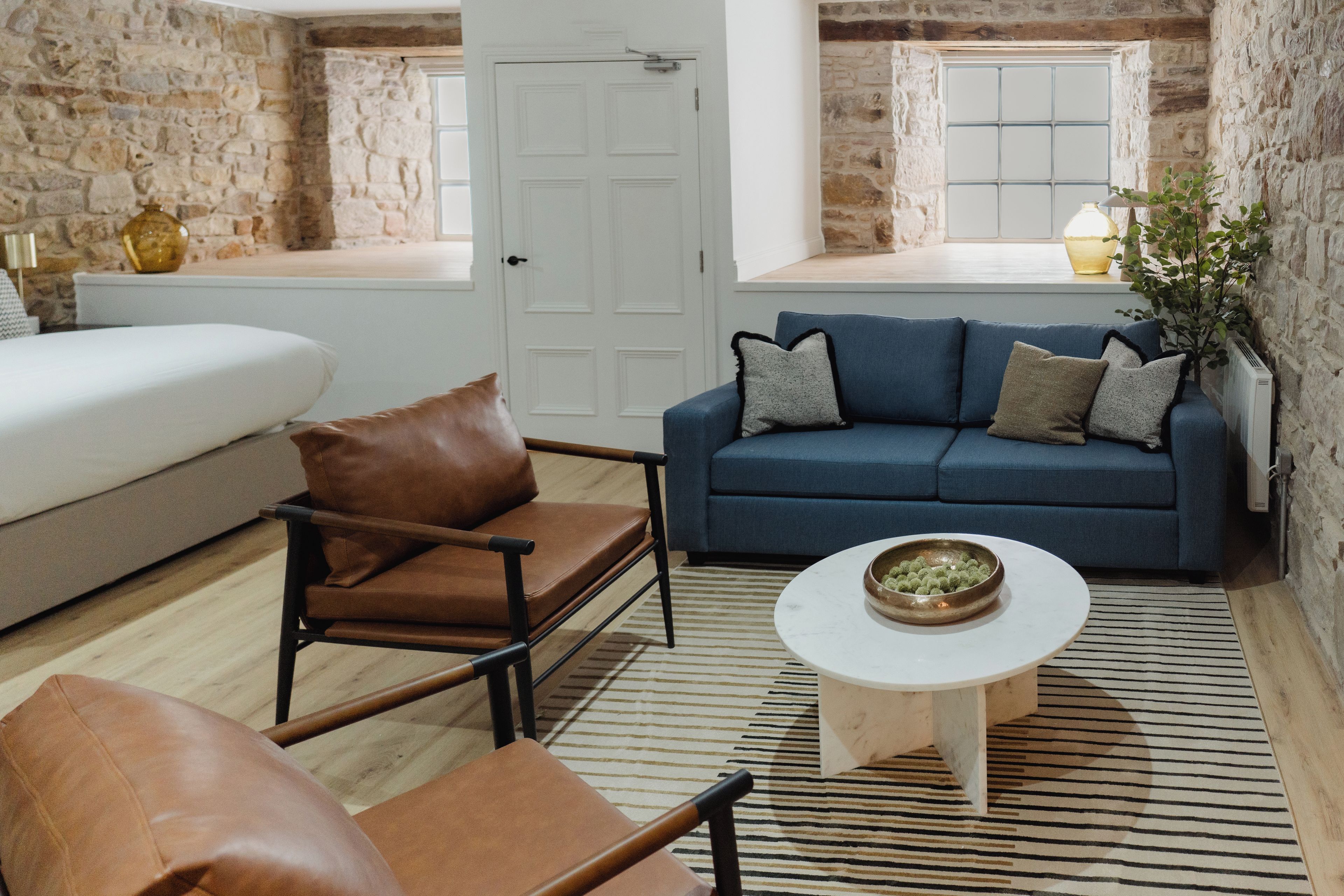 Sala de estar moderna com sofá, poltrona e mesa de centro, com paredes de pedra e vista pela janela.