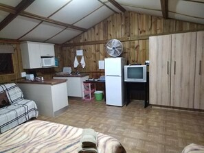 Quarto compacto com cozinha compacta, uma cama e um ventilador.