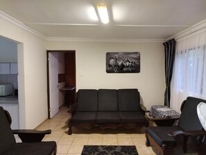 Uma sala de estar com sofá, uma poltrona, mesinha e uma obra de arte pendurada na parede.