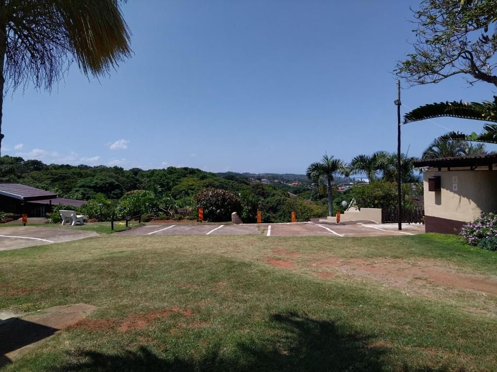 Uma área de estacionamento com um gramado à frente, um edifício com telhado vermelho e vista para uma paisagem montanhosa.