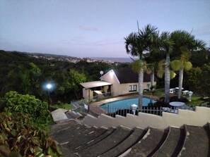Área da piscina com degraus que levam à água, cercada por palmeiras e vista para a paisagem.