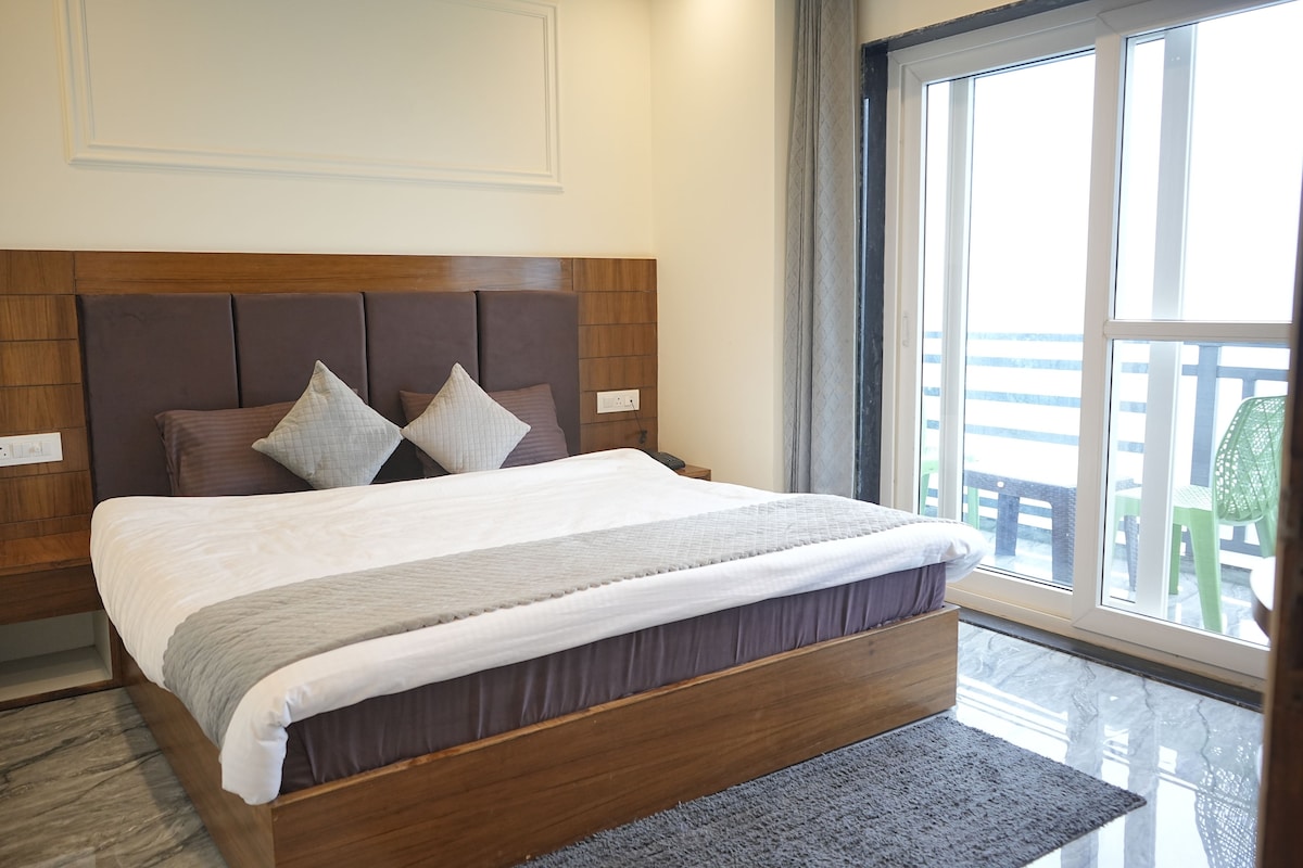 Quarto de hotel moderno com uma cama grande, cabeceira de madeira e vista para o exterior.
