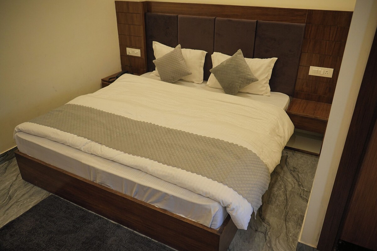 Cama bem arrumada com cabeceira de madeira, manta listrada em cinza e branco, e travesseiro cinza.