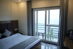 Quarto de hotel com uma cama grande, vista para a varanda e uma cafeteira no criado-mudo.