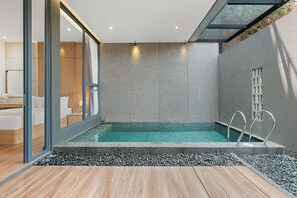 Piscina interior moderna com parede de vidro, piso de madeira e borda de pedras.