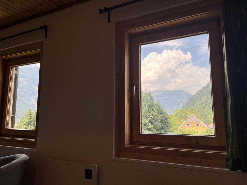 Quarto com duas janelas, uma das quais oferece vista para uma paisagem montanhosa e um edifício.