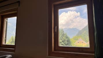 Quarto com duas janelas, uma das quais oferece vista para uma paisagem montanhosa e um edifício.