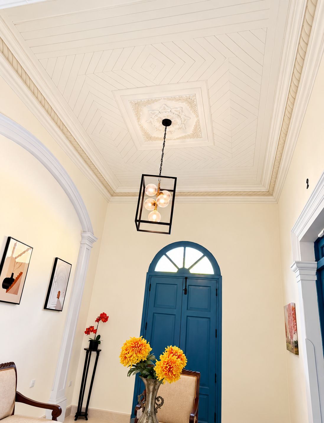 Um corredor com teto branco, porta azul e um vaso com flores.
