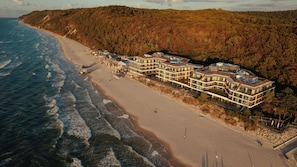 Um hotel à beira-mar com vários edifícios, praia e um morro coberto por vegetação.