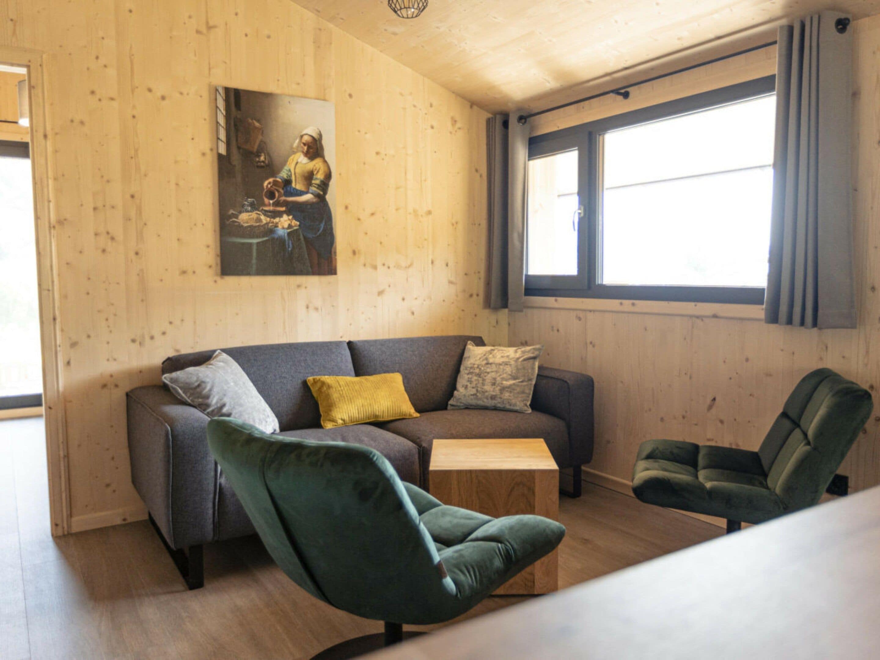 Sala de estar com parede de madeira, um sofá, uma poltrona verde, uma mesa de centro e um quadro.