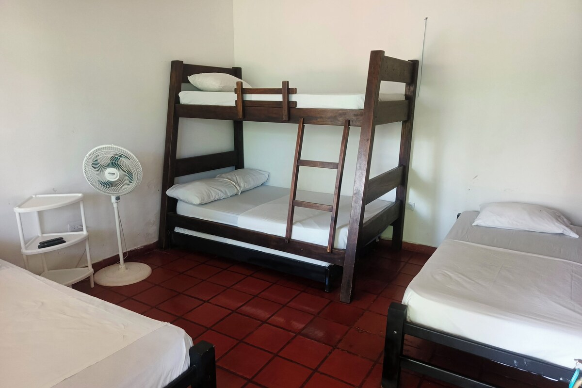 Quarto com duas beliches, um ventilador e uma estante branca.