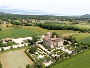 Um castelo com uma torre, rodeado por jardins bem cuidados e campos.