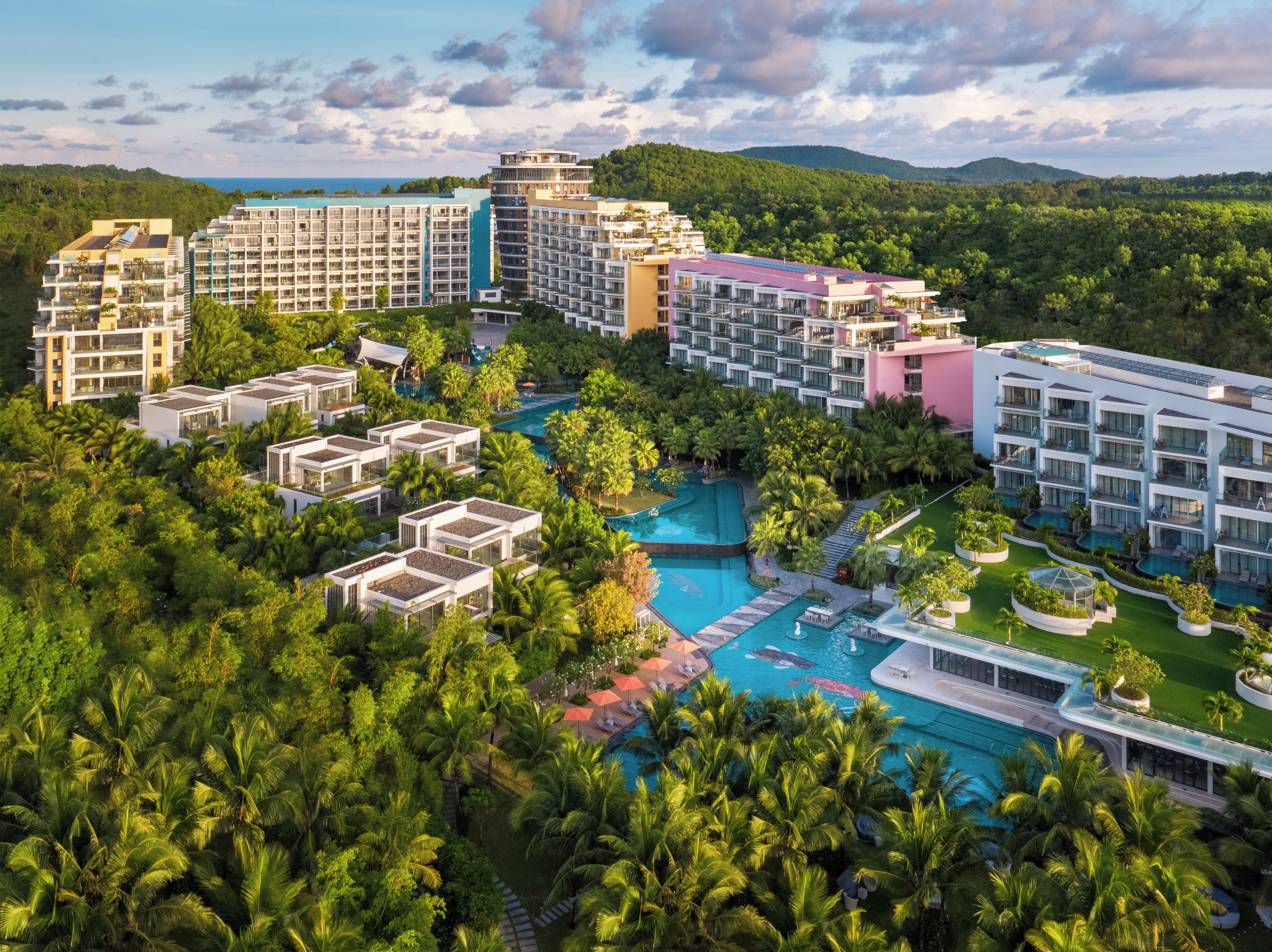 Resort com vários edifícios, piscina central e vegetação exuberante.