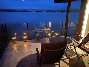 Terraço com vista para a água, mesa redonda e várias cadeiras.