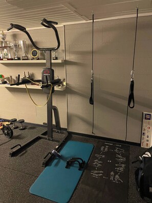 Uma academia doméstica com uma bicicleta ergométrica, halteres, um tapete de yoga e uma plataforma vibratória.