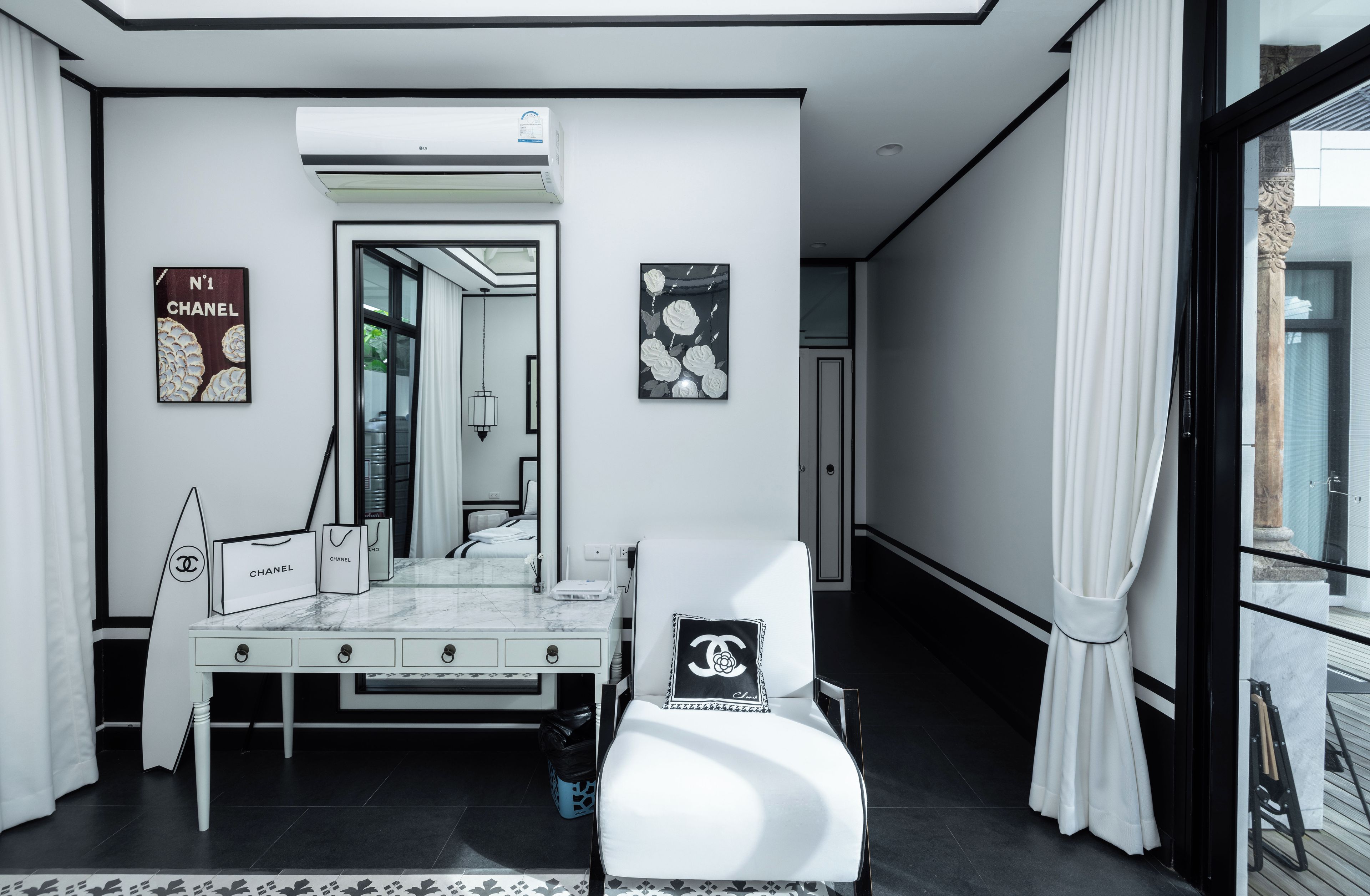Quarto de hotel moderno com um espelho grande, toucador branco e almofada com a marca Chanel.
