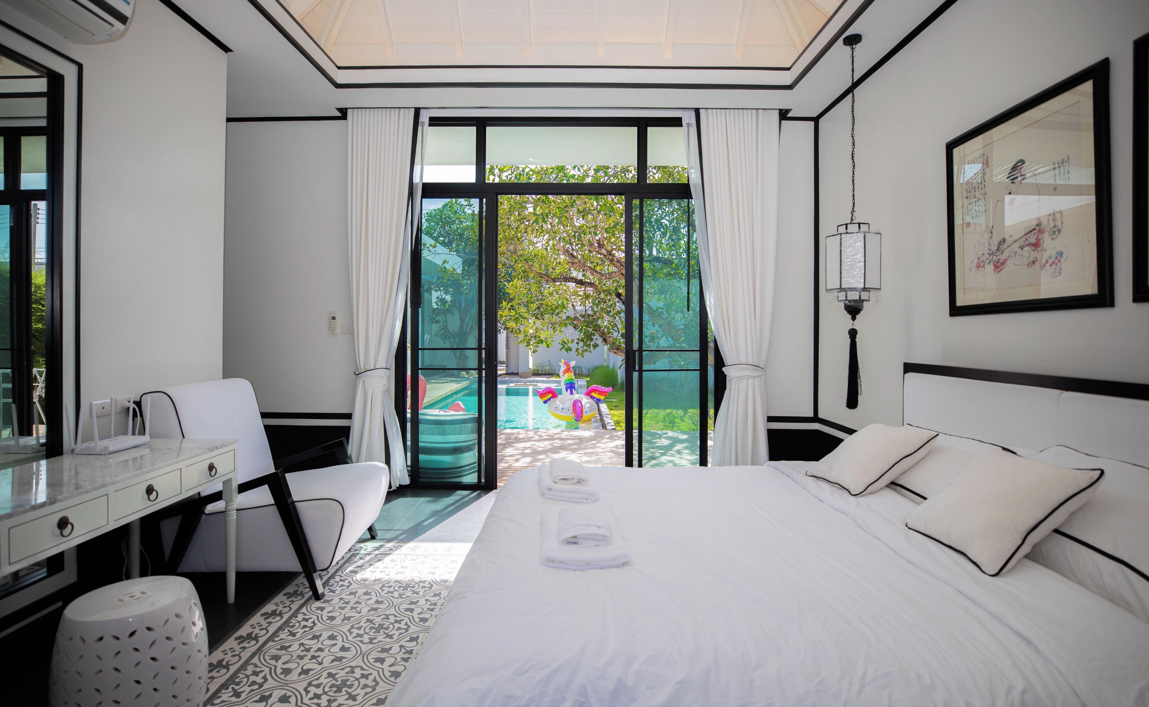 Quarto de hotel com cama, escrivaninha, cadeira e vista para uma piscina.