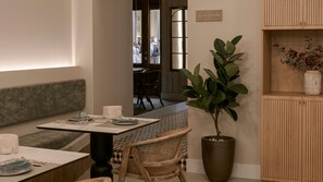Uma área de refeições com mesa posta para dois, um banco e um vaso de planta.
