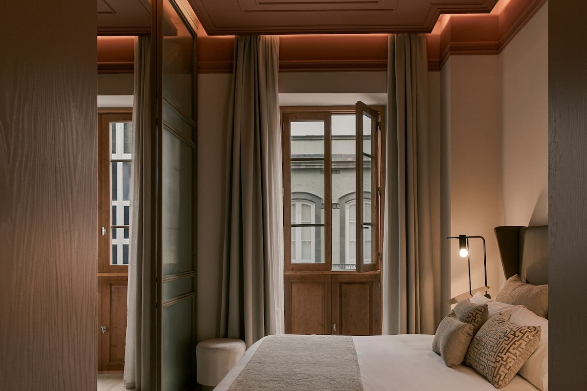 Quarto de hotel com cama, cortinas, janela e abajur.