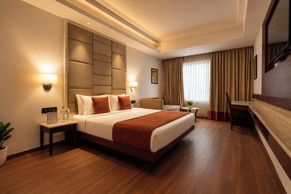 Quarto de hotel com uma cama grande, escrivaninha, cadeira, planta em vaso e televisão.