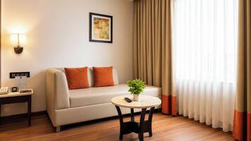 Quarto de hotel com sofá, uma mesinha com uma planta, luminária e um quadro na parede.