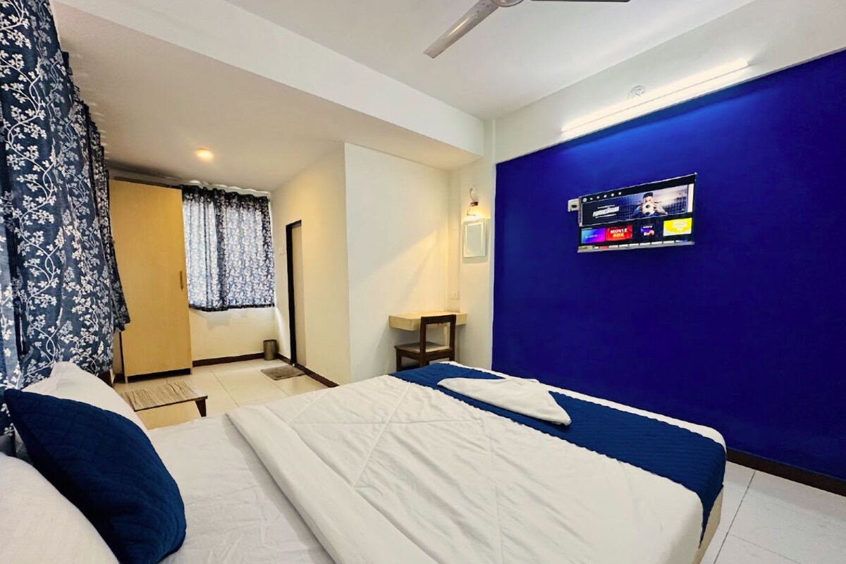 Quarto de hotel com cama, televisão fixada na parede e janela com cortinas.
