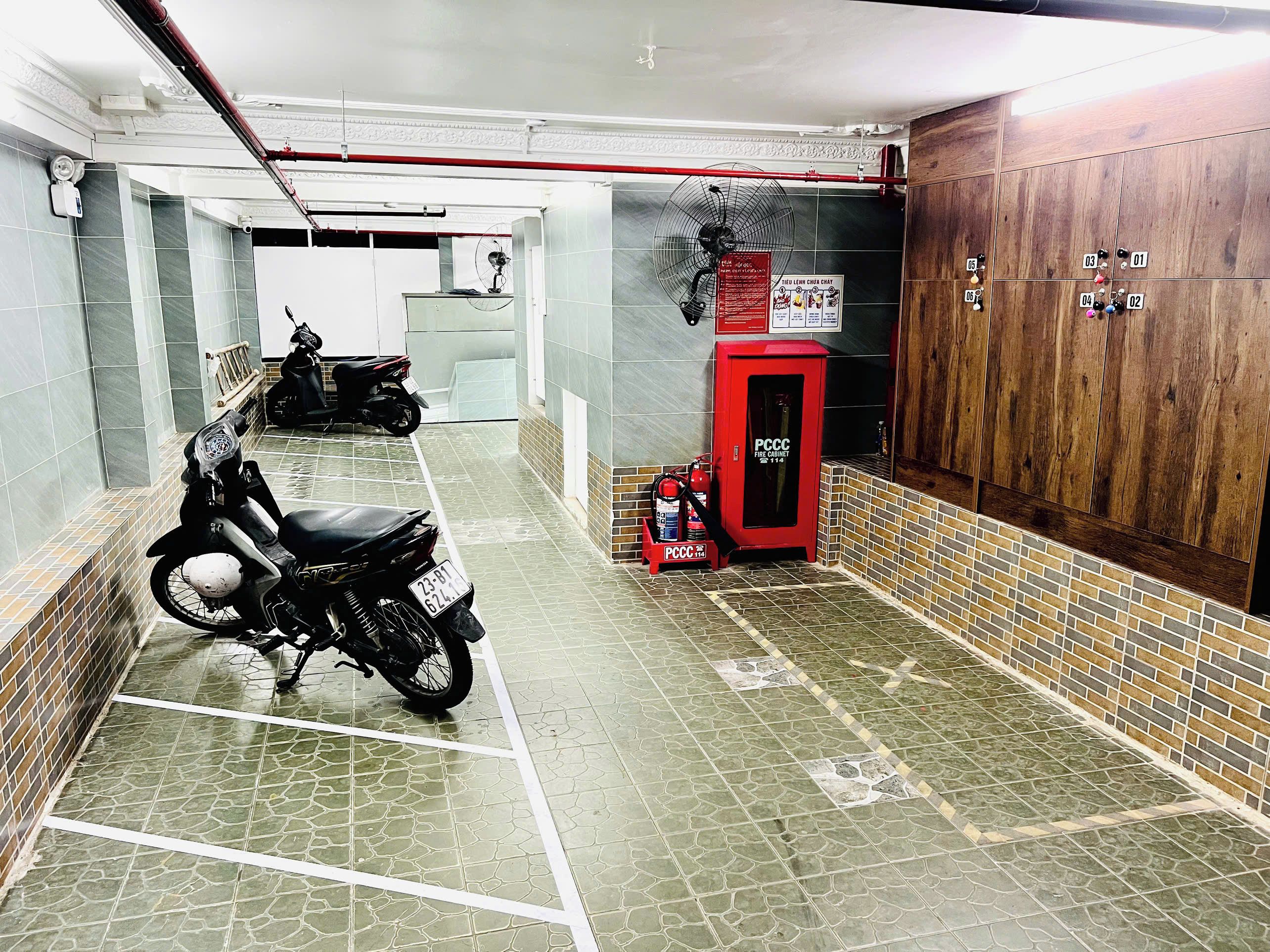 Uma área de estacionamento com duas motocicletas, um extintor de incêndio e um armário com uma placa.