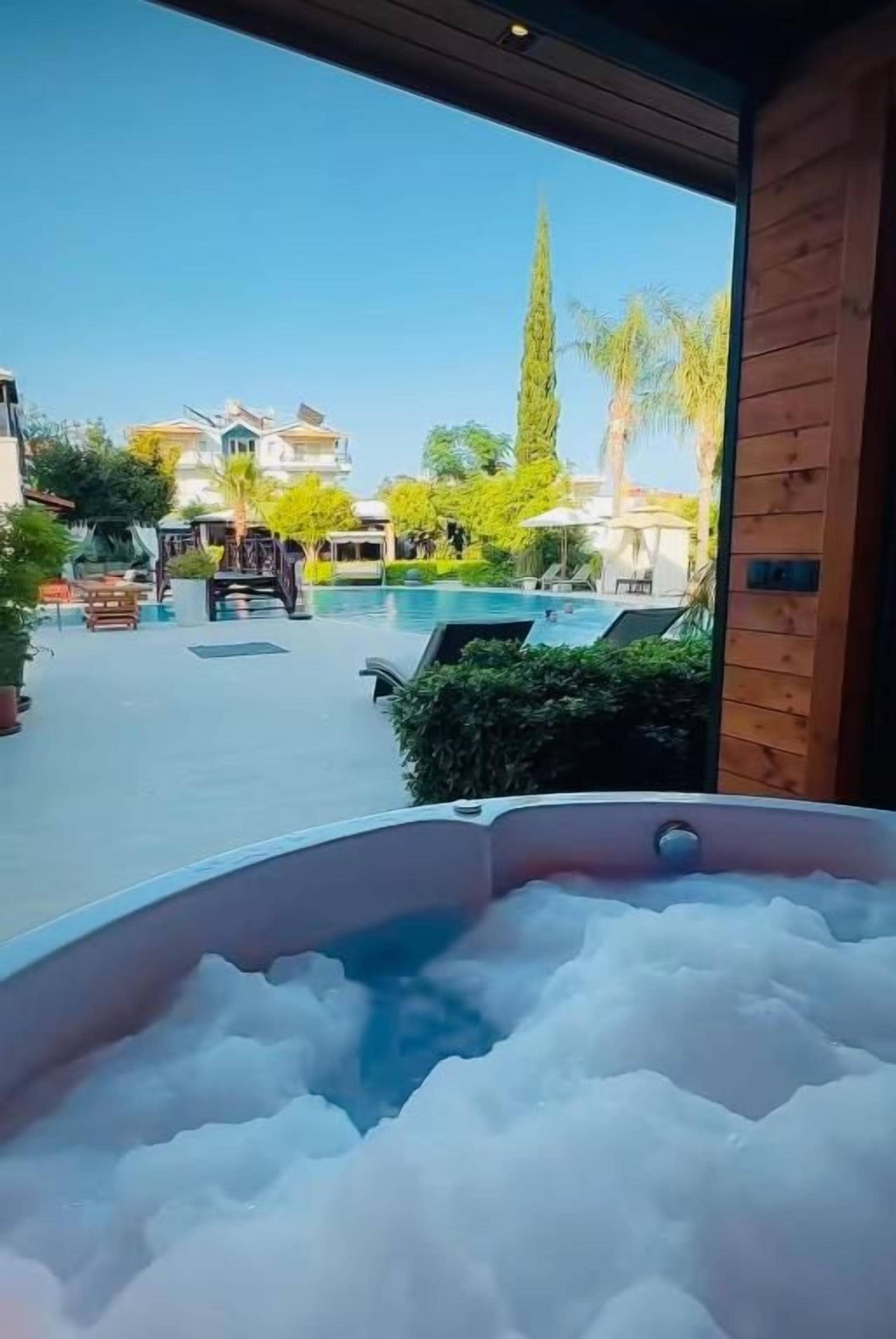 Uma banheira de hidromassagem com vista para uma piscina e vegetação ao redor.