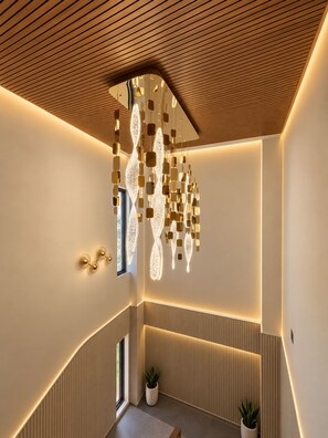 Um interior moderno com teto inclinado, iluminação embutida e luminária decorativa.