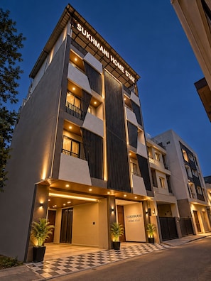 Um hotel com vários andares e design moderno, com uma placa grande indicando 'SUKHMANI HOME STAY' no topo.