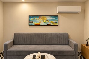 Um sofá cinzento com uma mesa de centro de mármore, um ar condicionado e uma obra de arte emoldurada na parede.