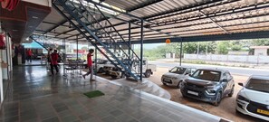 Área de estacionamento coberta com escadas que levam a um nível superior, alguns carros estacionados e uma pessoa caminhando.