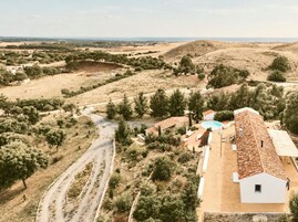 Paisagem rural com estrada sinuosa, um edifício branco com telhado de telhas e piscina.