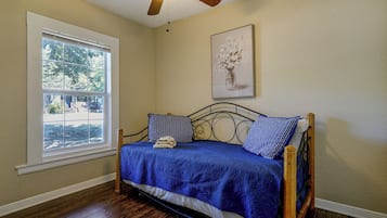 Quarto com cama de madeira, janela, ventilador de teto e um quadro na parede.