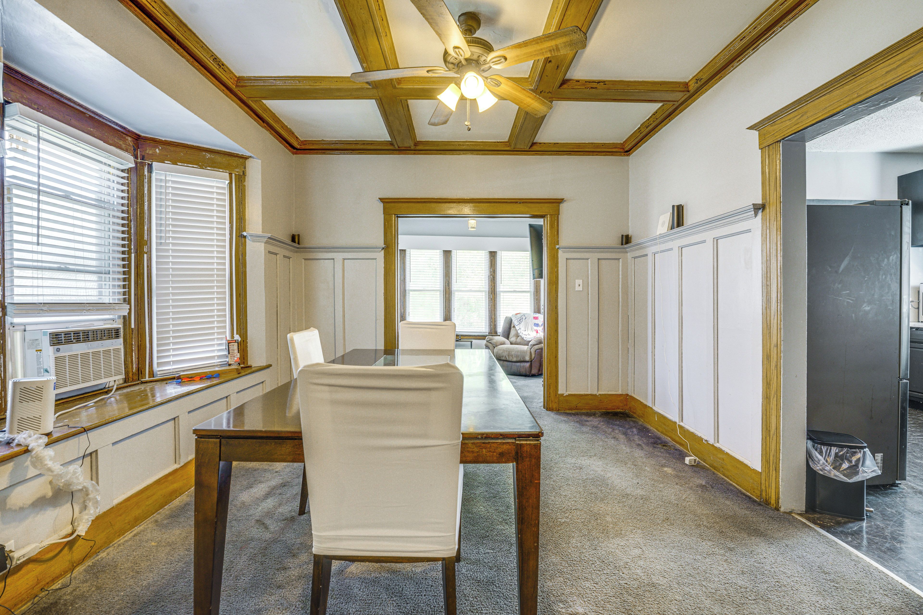 Uma sala de jantar com mesa e cadeiras de madeira, um ventilador de teto e vista para outro ambiente.